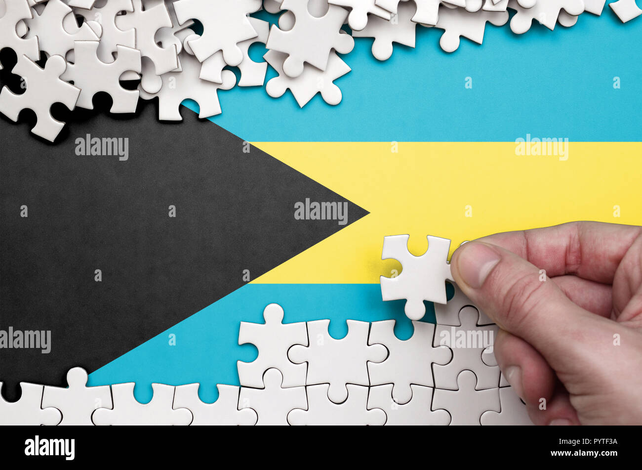 Bahamas flag is depicted on a table on which the human hand folds a ...