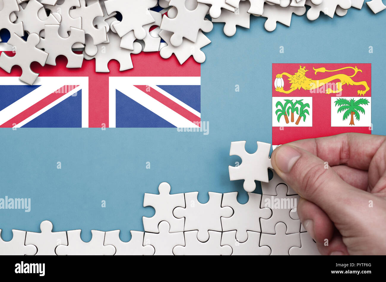 Fiji flag is depicted on a table on which the human hand folds a puzzle ...
