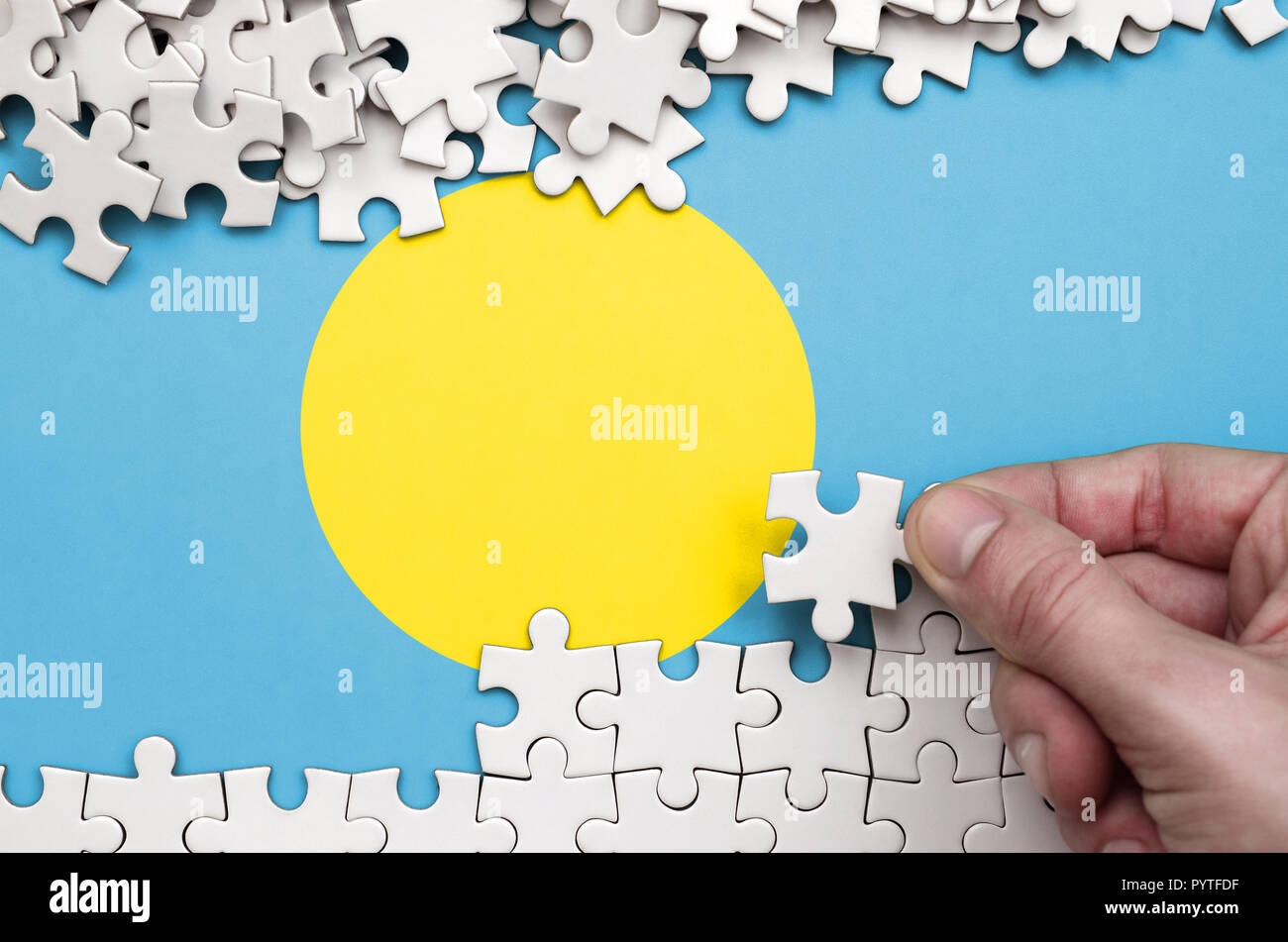 Palau flag is depicted on a table on which the human hand folds a ...