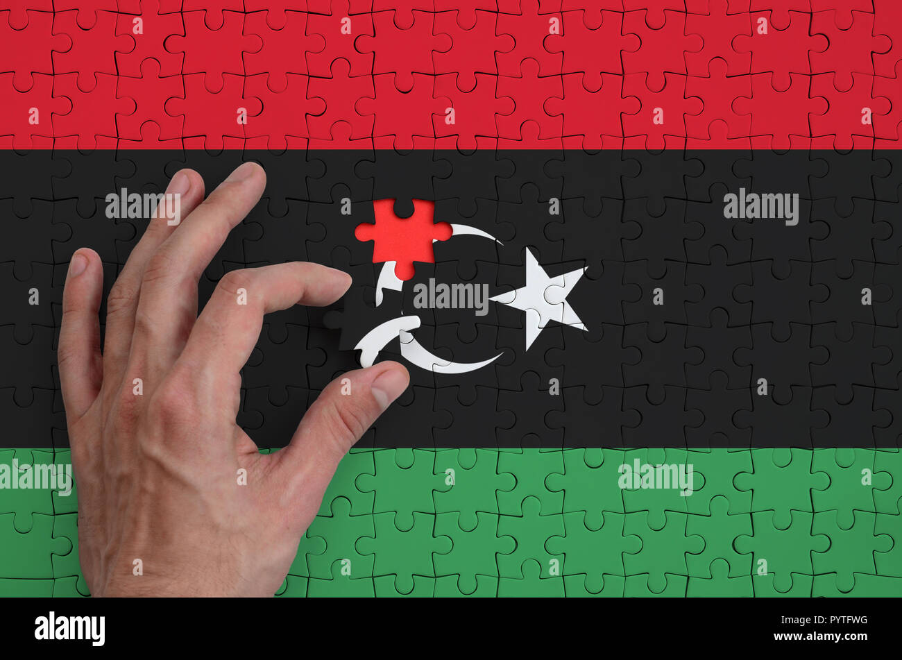 Libya flag is depicted on a puzzle, which the man's hand completes to ...