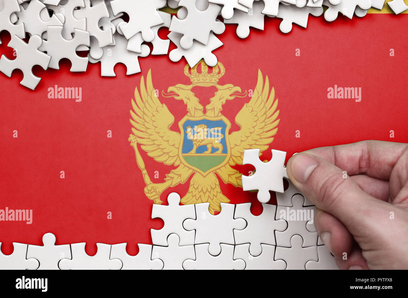 Montenegro flag is depicted on a table on which the human hand folds a ...