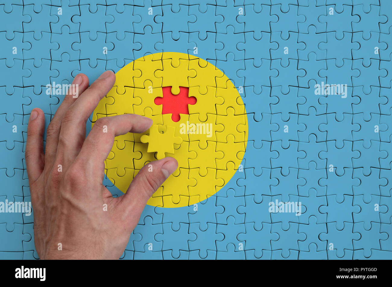 Palau flag is depicted on a puzzle, which the man's hand completes to ...