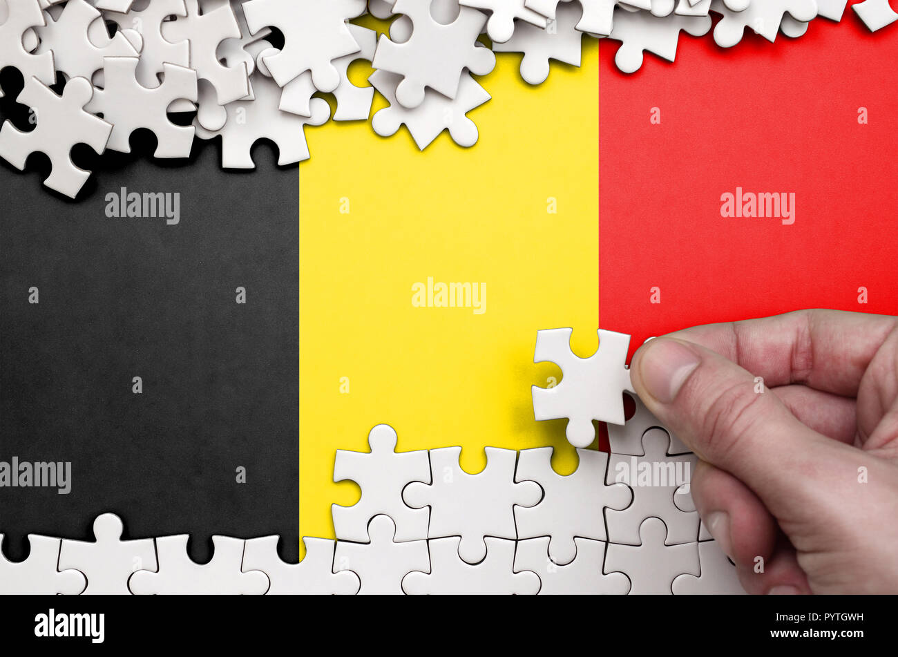 Belgium flag is depicted on a table on which the human hand folds a ...