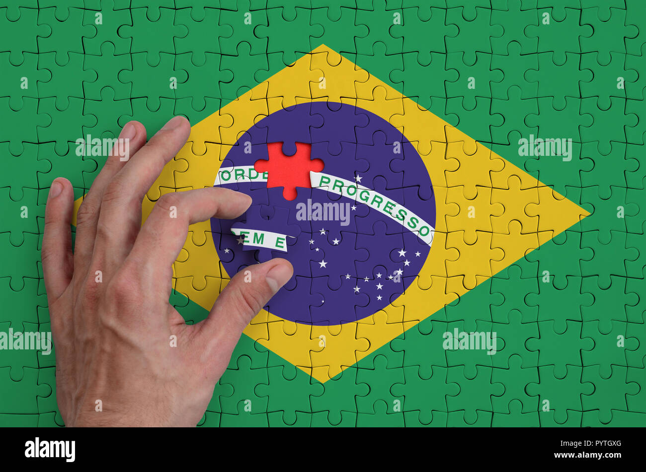 Brazil flag is depicted on a puzzle, which the man's hand completes to ...
