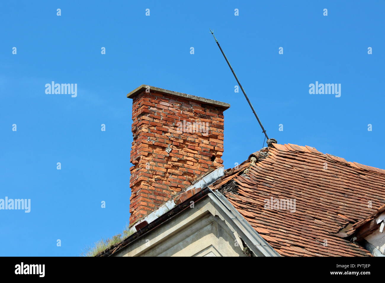 Cracked broken red brick chimney next to metal leaning lightning rod on ...