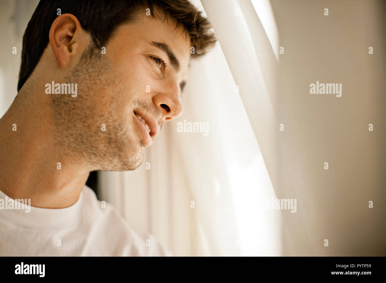 Young man looking through a window from inside his home Stock Photo - Alamy