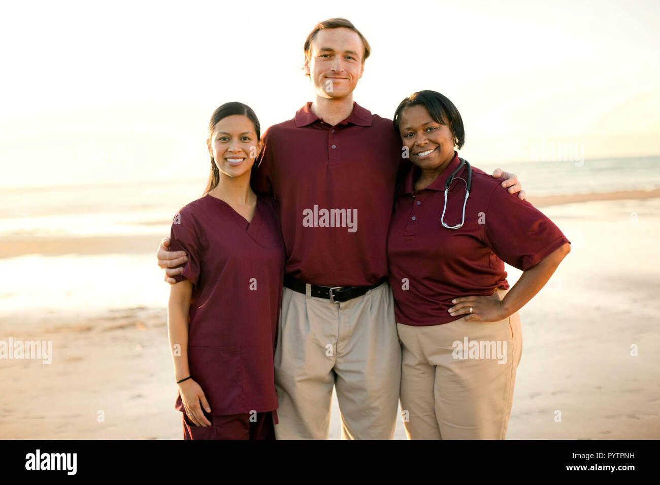 Portrait of three smiling nurses standing side by side on a beach with ...