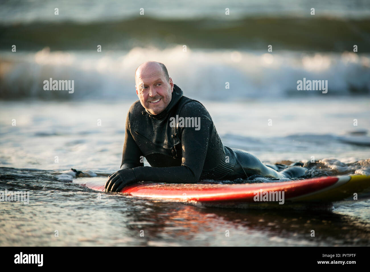 Smiling mid adult man in a wetsuit floating on his surfboard in the sea ...