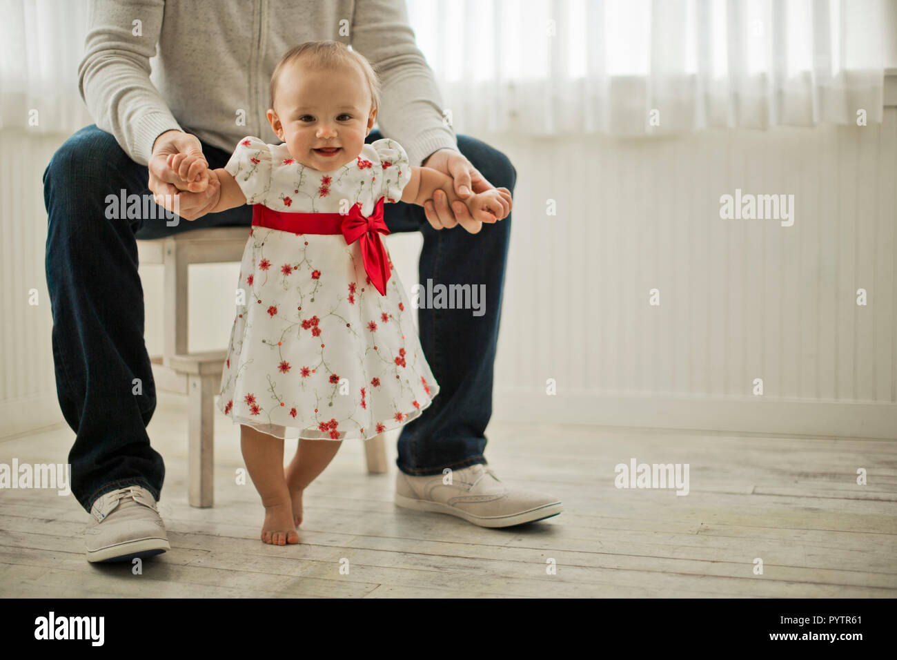 Portrait of a smiling baby girl taking her first steps assisted by her ...