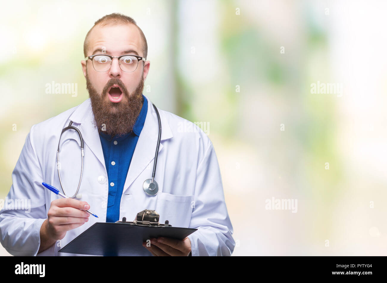 Young doctor man holding clipboard over isolated background scared in ...