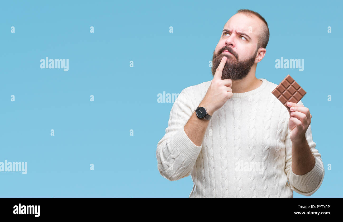 Young hipster man eating chocolate bar over isolated background serious ...