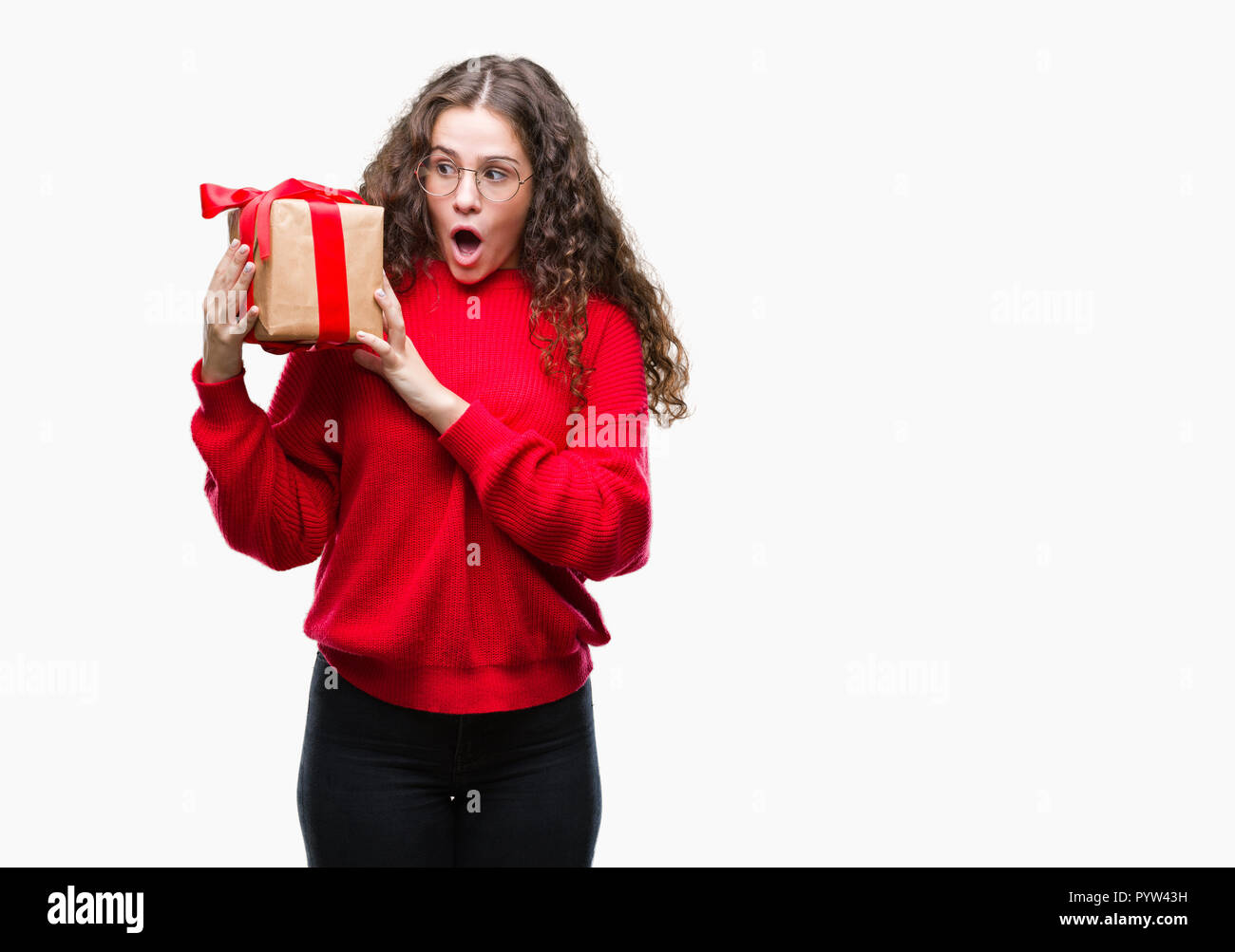 Young brunette girl holding a gift over isolated background scared in ...