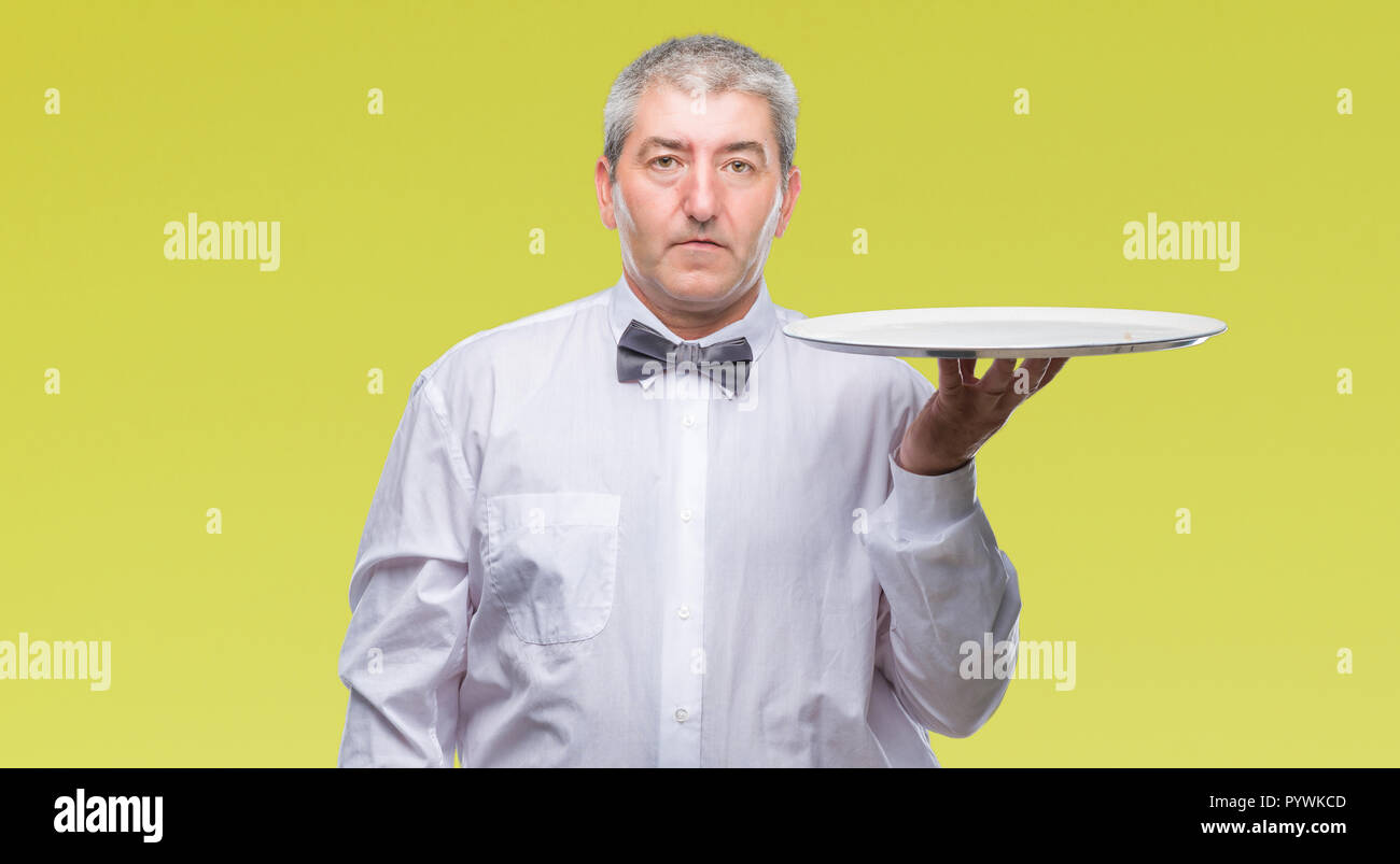 Handsome senior waiter man holding silver tray over isolated background ...