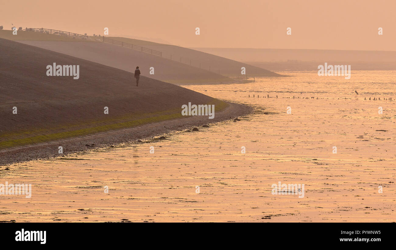 Person walking on Delta works Sea dike of the Waddensea in orange haze ...