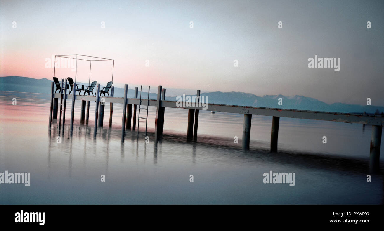 A pier over a tranquil lake with seating arrangement Stock Photo - Alamy