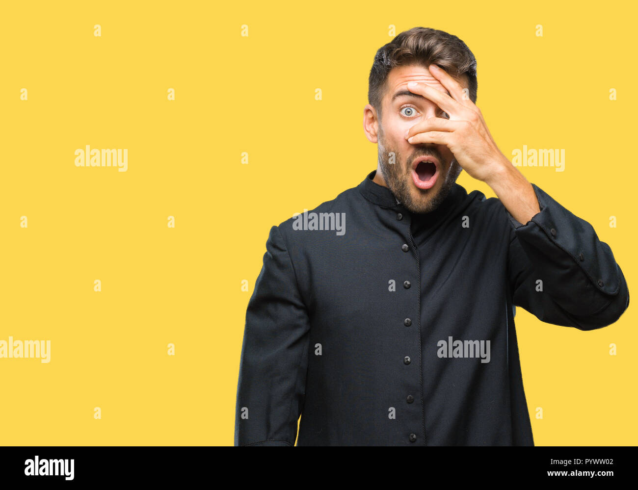 Young catholic christian priest man over isolated background peeking in ...