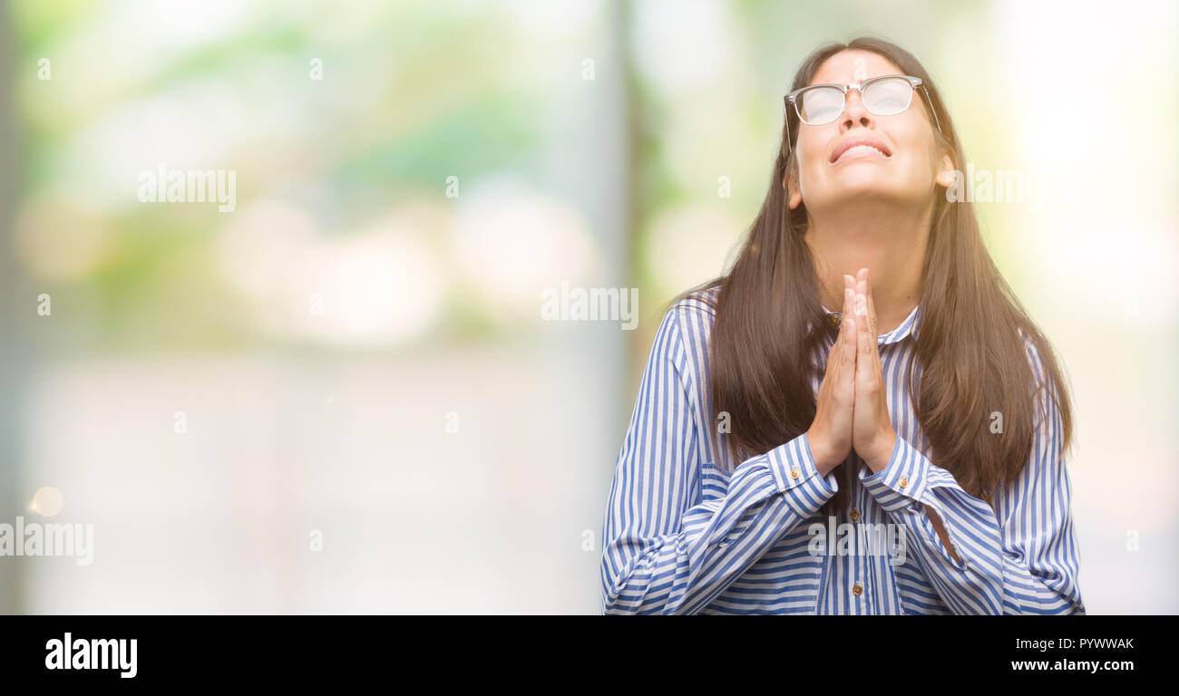 Young beautiful hispanic business woman begging and praying with hands ...