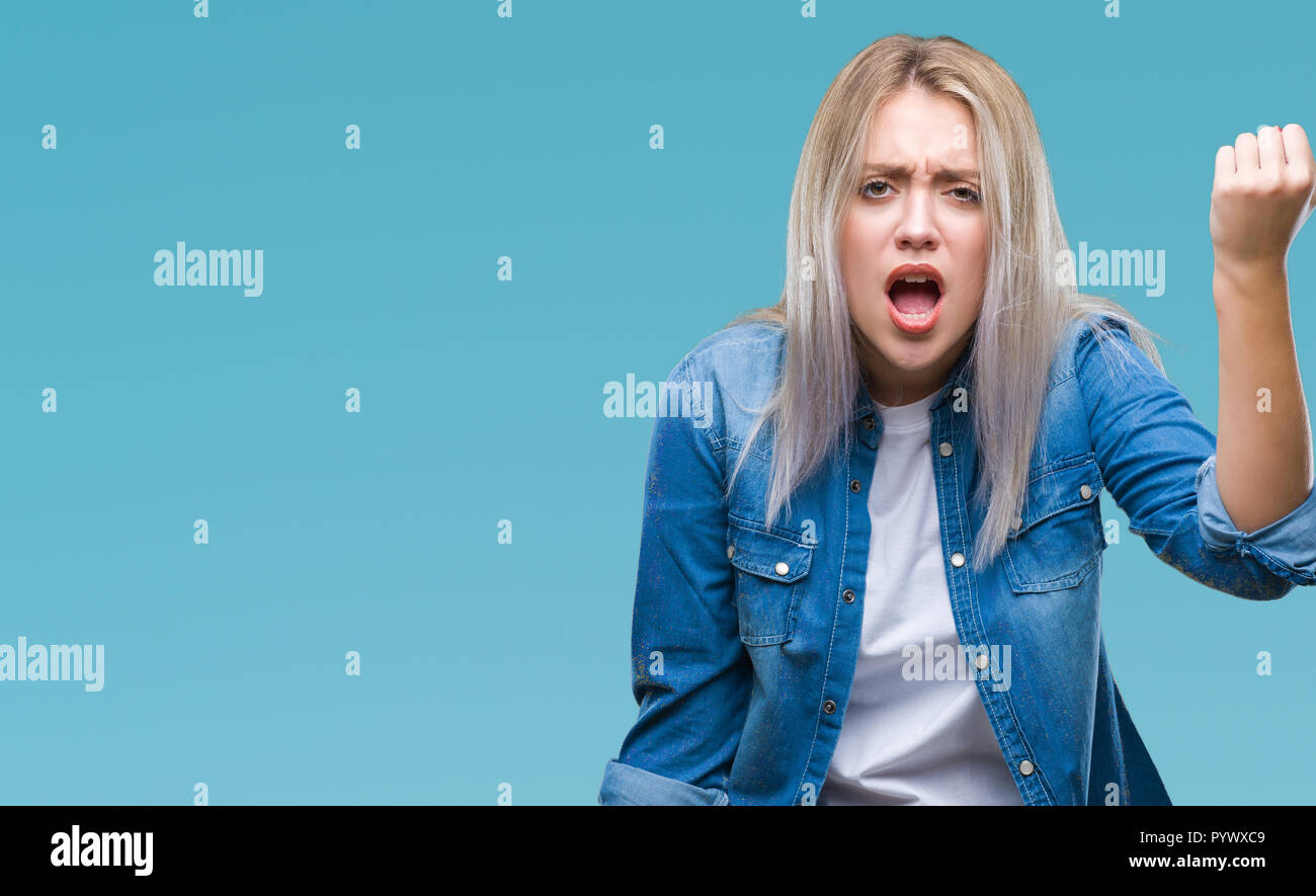 Young blonde woman over isolated background angry and mad raising fist ...