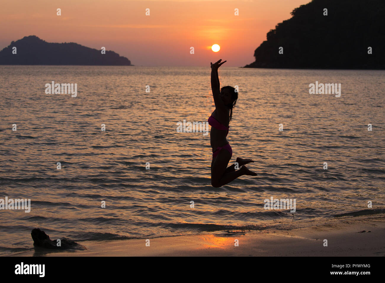 Woman jumping on a tropical beach at sunset to reach the sun, Thailand ...