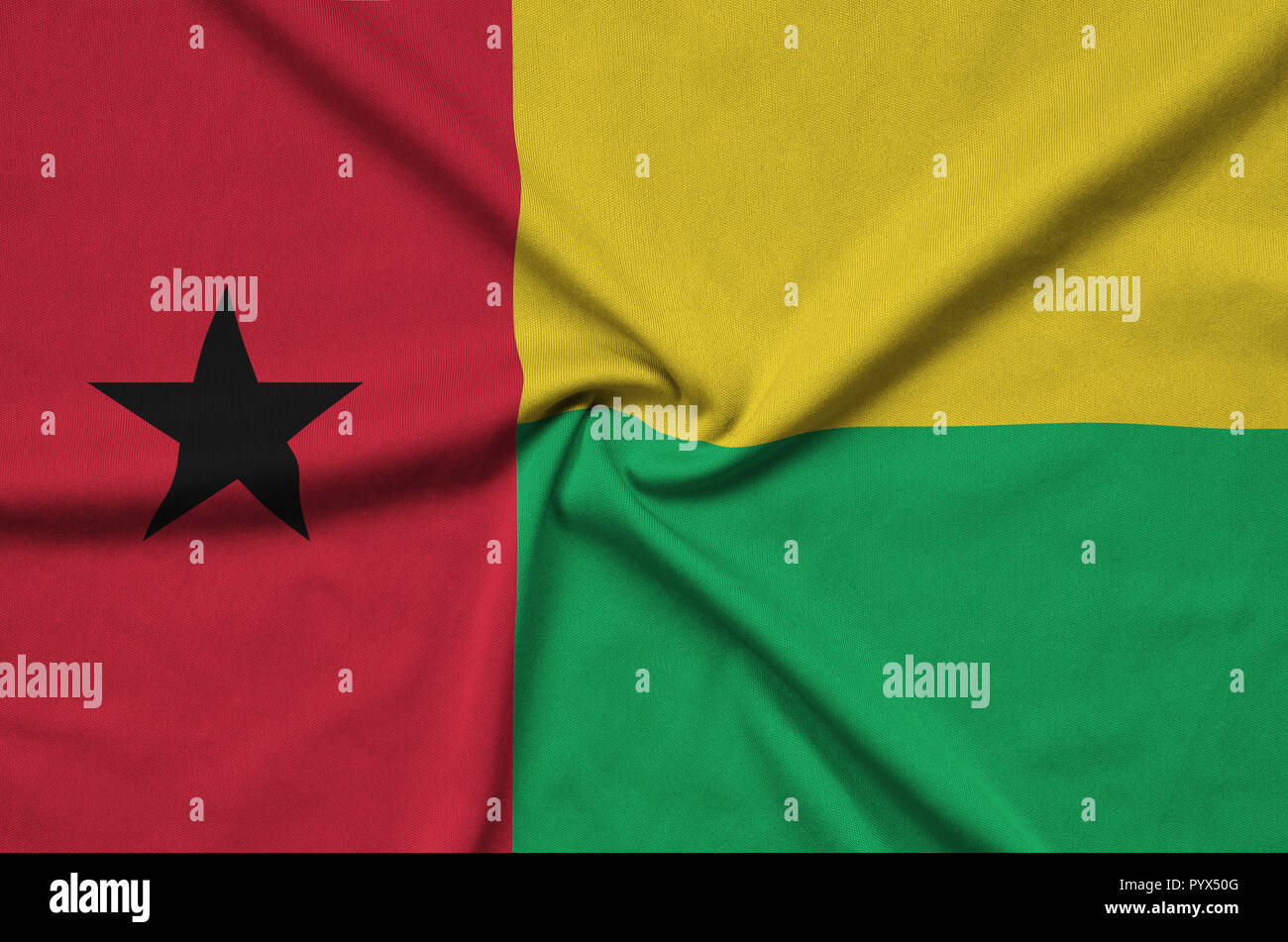 Guinea Bissau flag is depicted on a sports cloth fabric with many folds ...