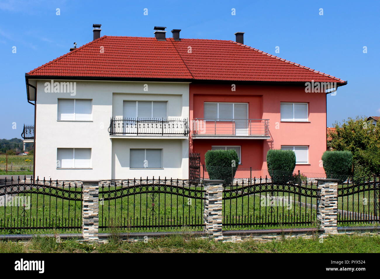 Two new white and dark pink attached suburban family houses with wrought iron fence on balcony ...