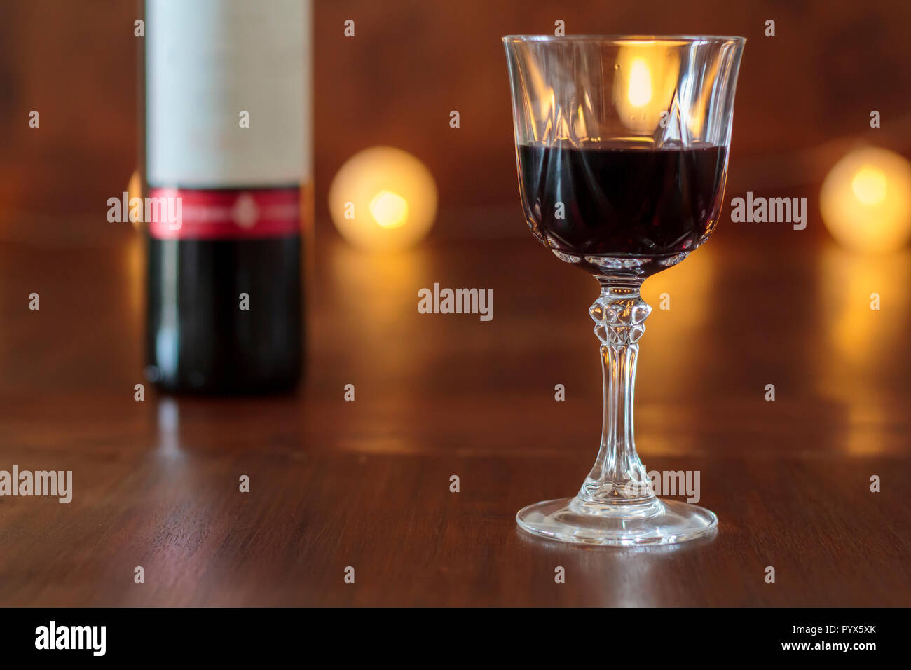 Glass of red wine on wooden table with the bottle in the background ...