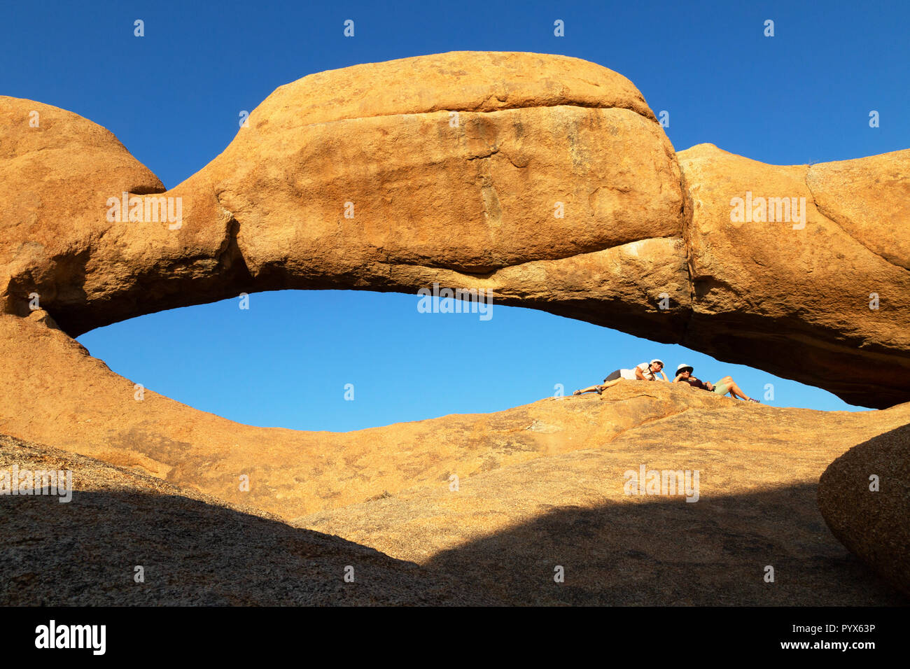 Namibia landscape; two tourists posing at the rock arch at Spitzkoppe ...