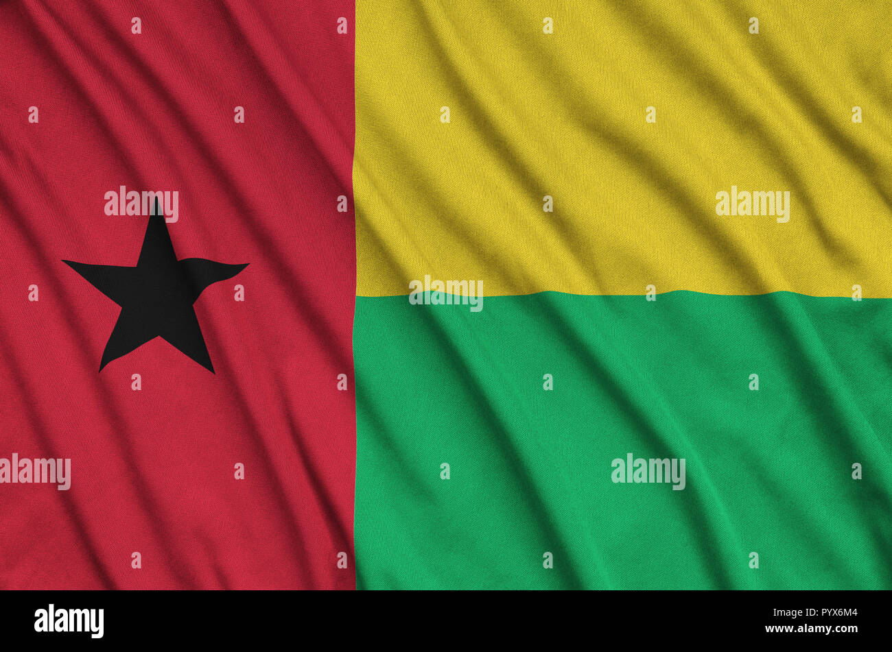 Guinea Bissau flag is depicted on a sports cloth fabric with many folds ...