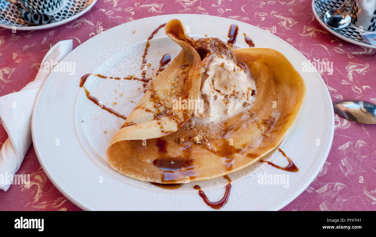 Crepe mit Haselnuss Eiscreme und Fruchsoße auf einem weißen Teller ...