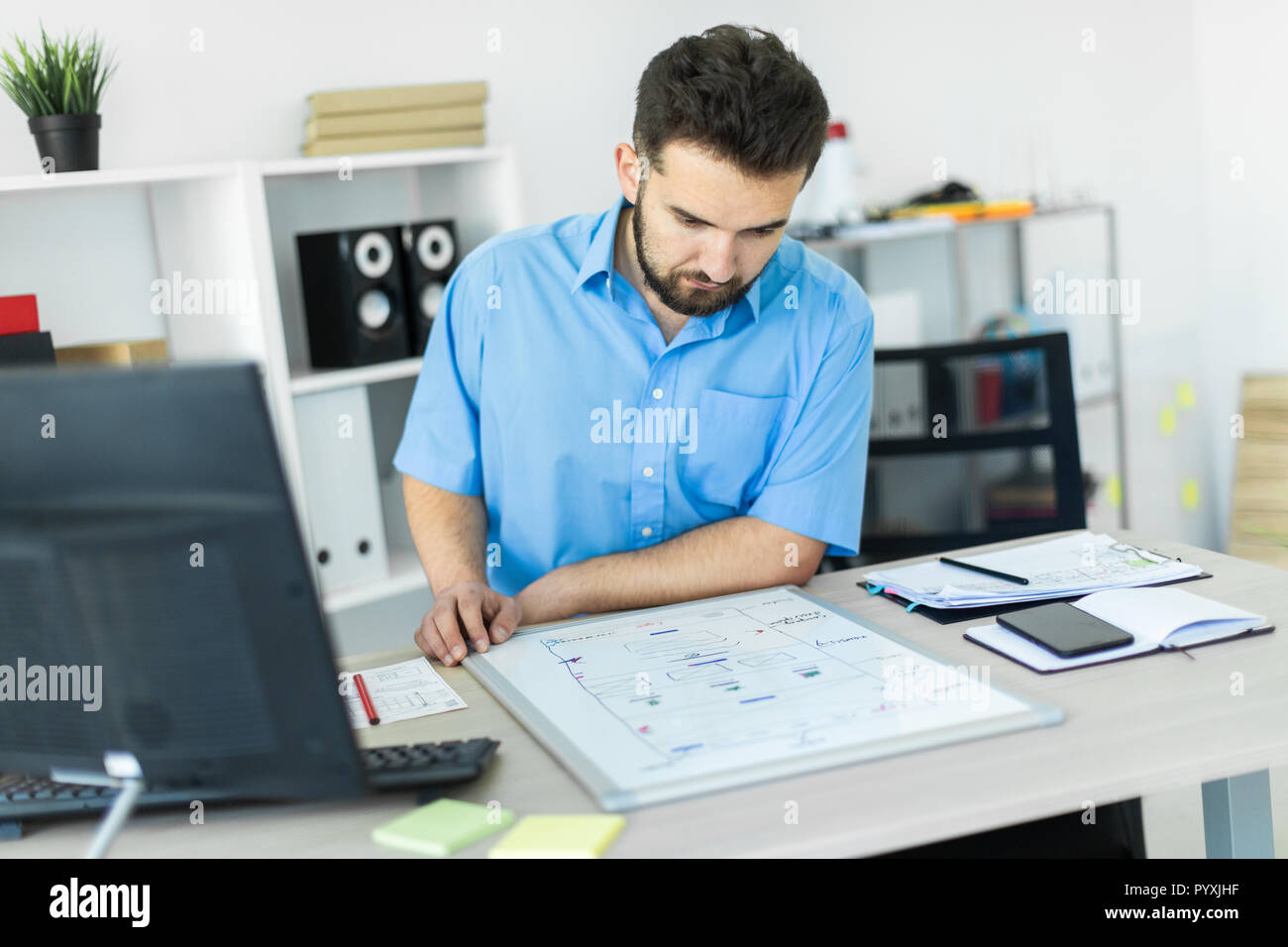 A young man standing in the office at a computer Desk and working with ...