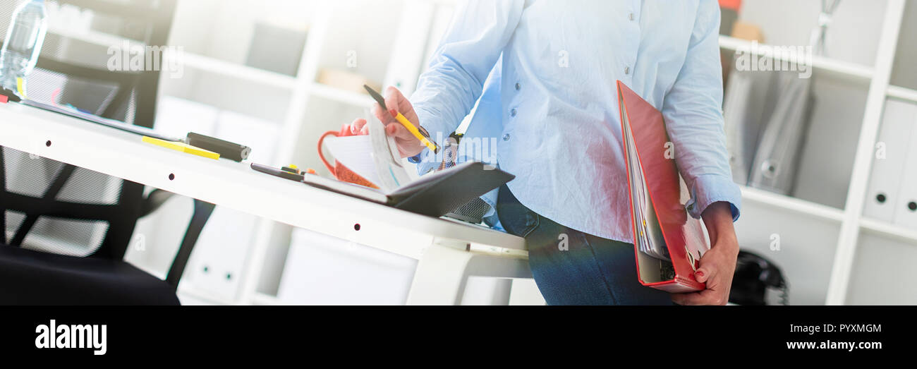A young girl in the office is standing, leaning on a table, and writing ...