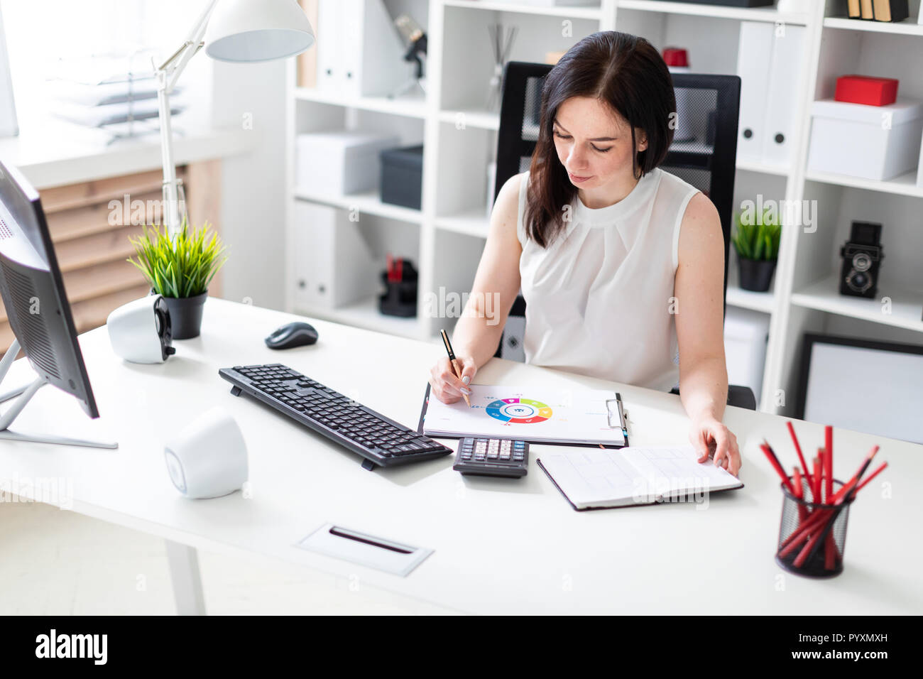 A young girl sitting in the office at a computer Desk and working with ...