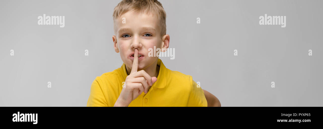 Portrait of cute little blonde caucasian boy in yellow t-shirt showing ...