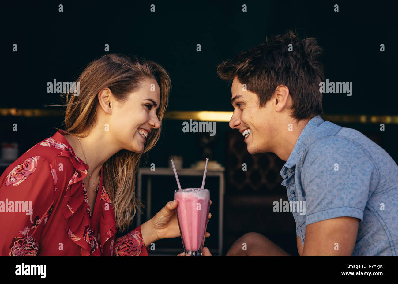 Romantic couple on a date sitting outdoors sharing a milkshake with two ...
