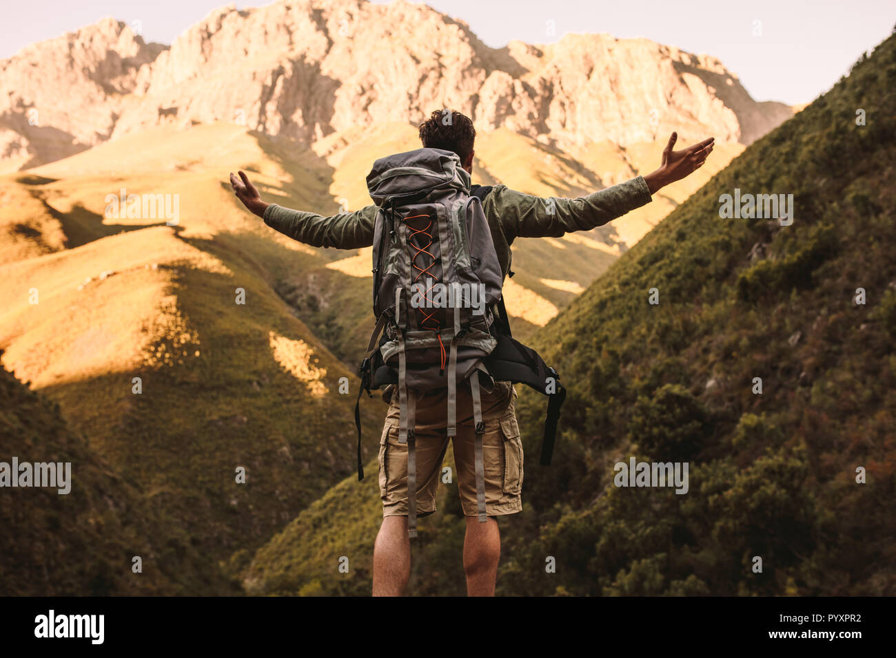 Rear view of young man with backpack standing with his arms ...