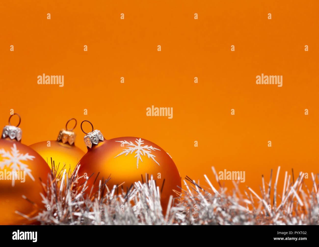 Three orange bauble Christmas decorations close up against an orange ...