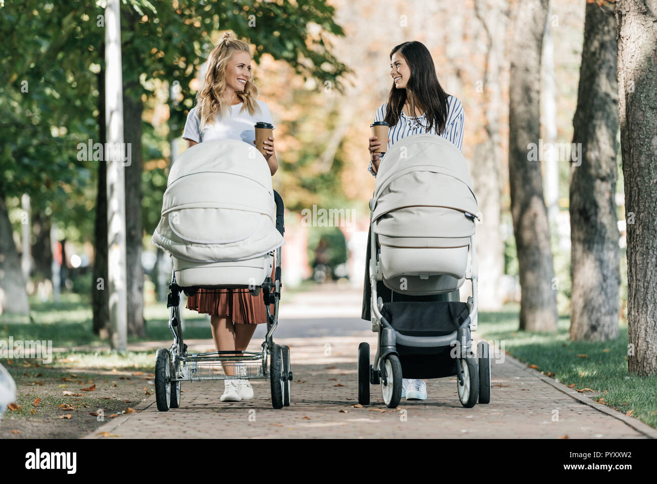 mothers walking with baby strollers and coffee to go in park and ...