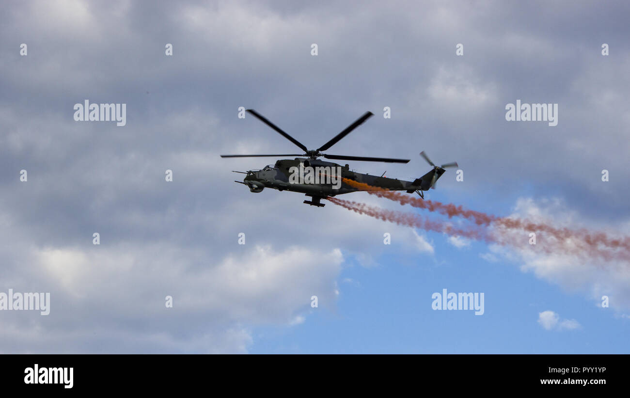 Combat helicopter with red smoke on blue sky with white clouds. View ...