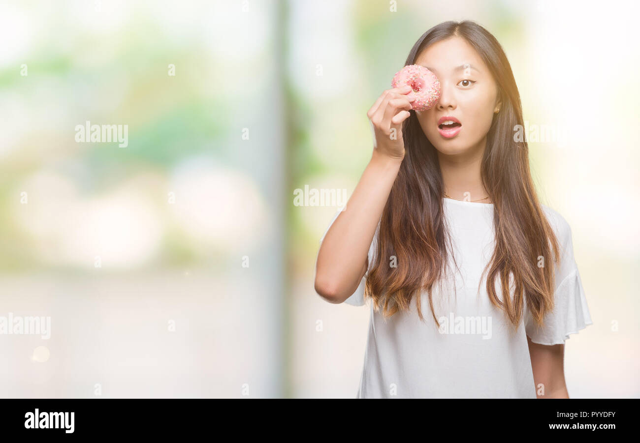 Young asian woman eating donut over isolated background scared in shock ...