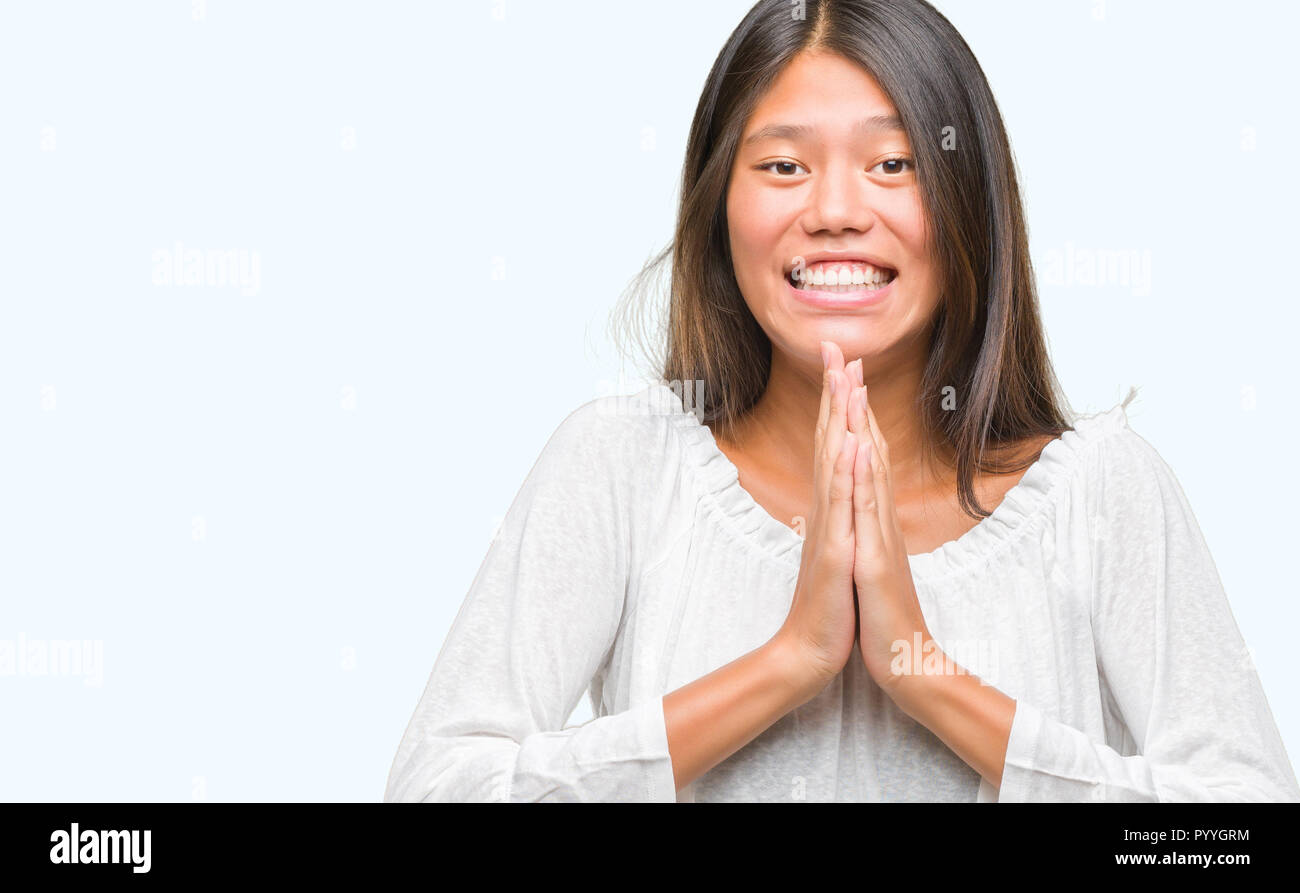 Young asian woman over isolated background praying with hands together ...