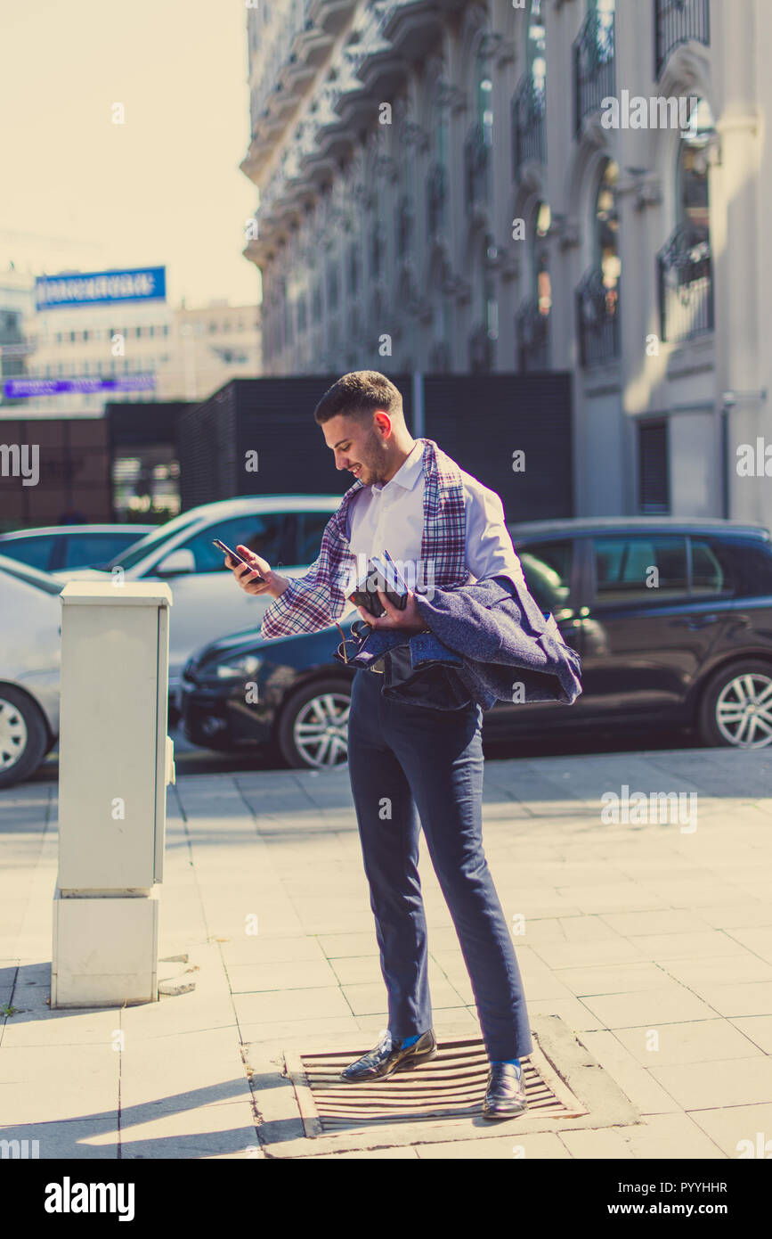 An urban man is in public, standing on the street and looking at his ...