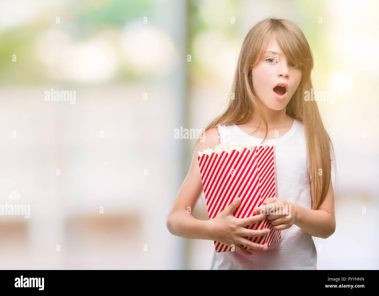 Young blonde toddler holding popcorn pack scared in shock with a ...