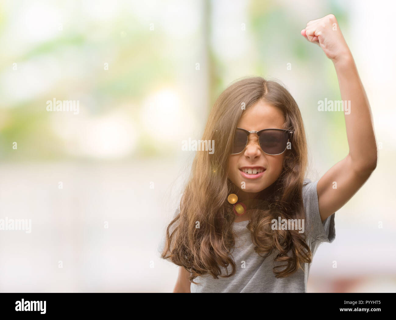 Brunette hispanic girl wearing sunglasses angry and mad raising fist frustrated and furious ...