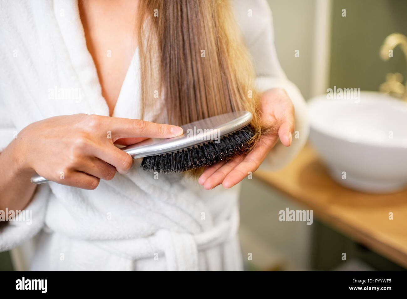 Woman combing hair with brush in the bathroom, close-up view with no ...