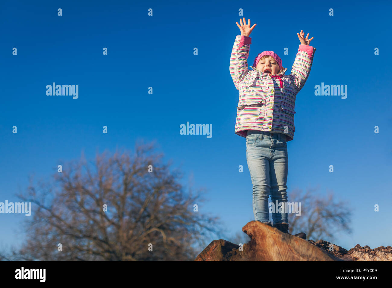 Cute little girl shouting from joy while standing on the top of large ...