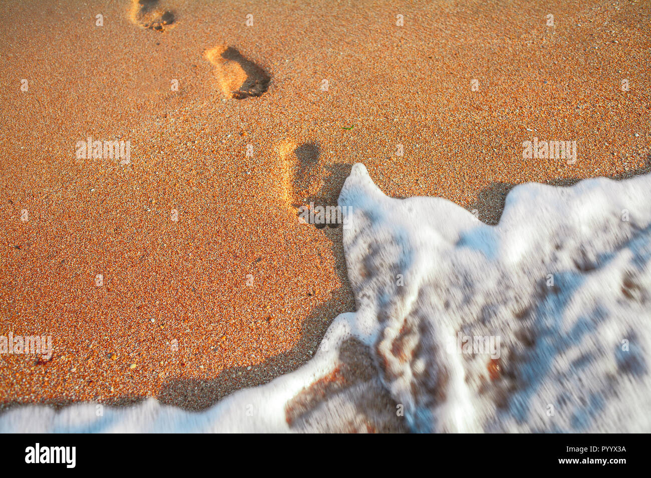 Footstep on red sand leadind into the water, blurred fast sea surf ...