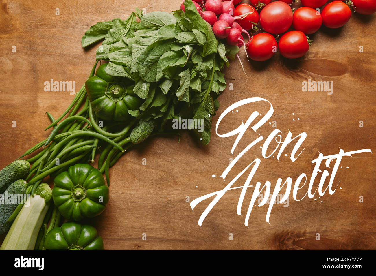 Green and red summer vegetables on wooden table with "bon appetit ...