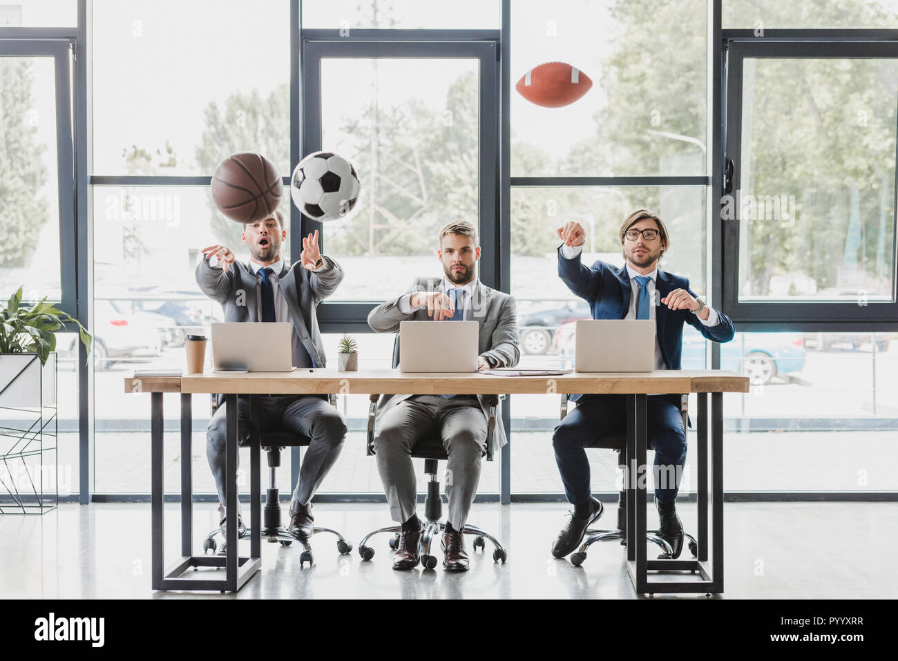 young office workers throwing balls while working with laptops in ...
