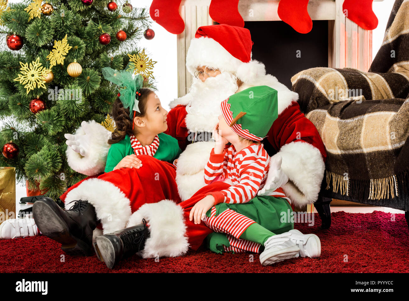 santa embracing kids while they sitting on floor in front of fireplace ...