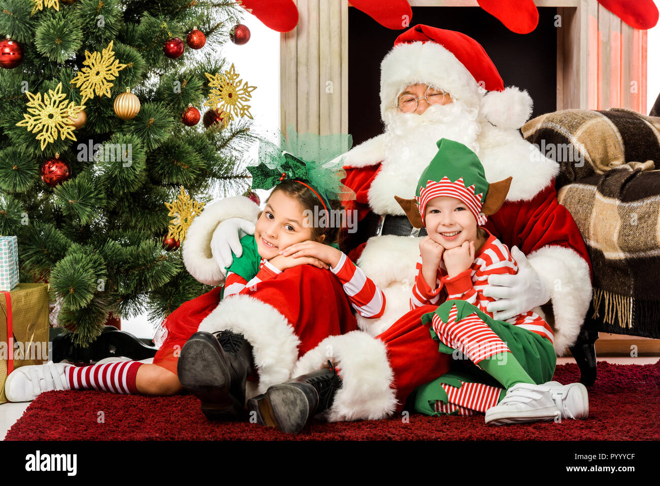 santa embracing happy kids while they sitting on floor in front of ...